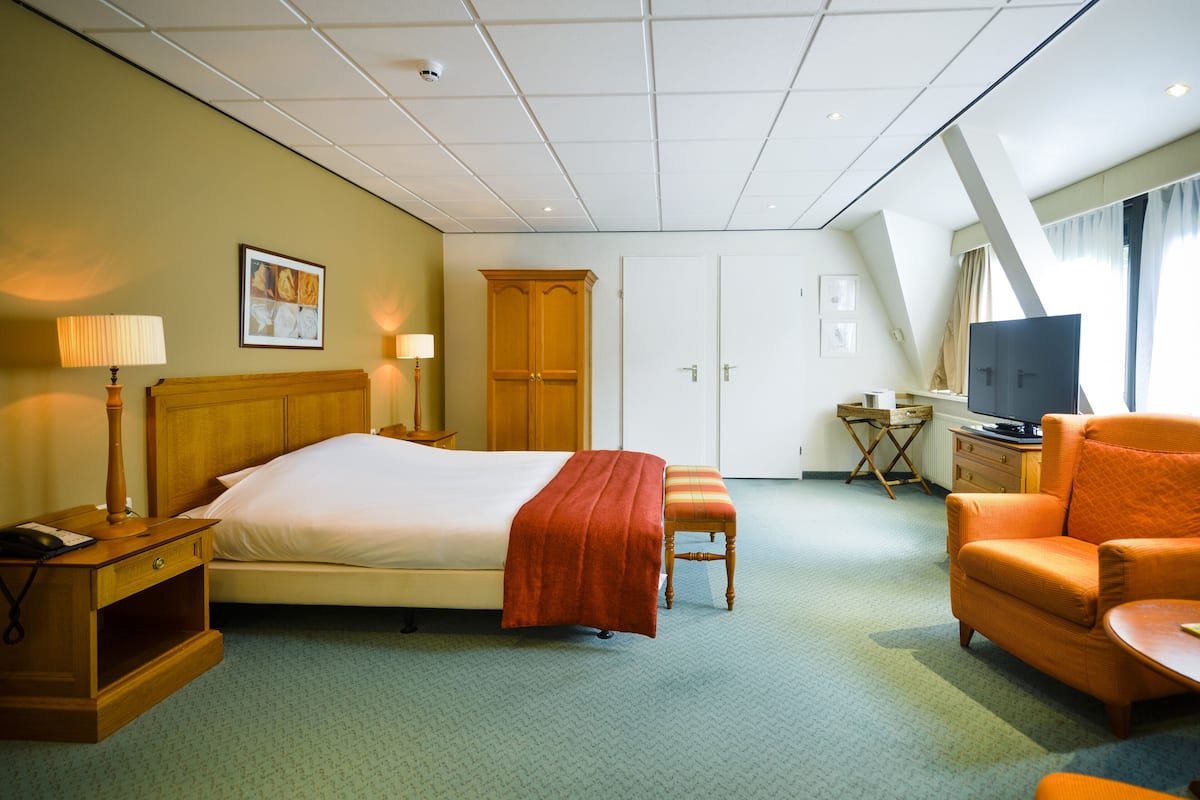 Quarto de hotel com cama, escrivaninha, televisão e uma cadeira.