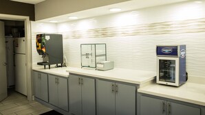 Cozinha com armários cinzas, bancada branca, geladeira, cafeteira e dispensador de água.