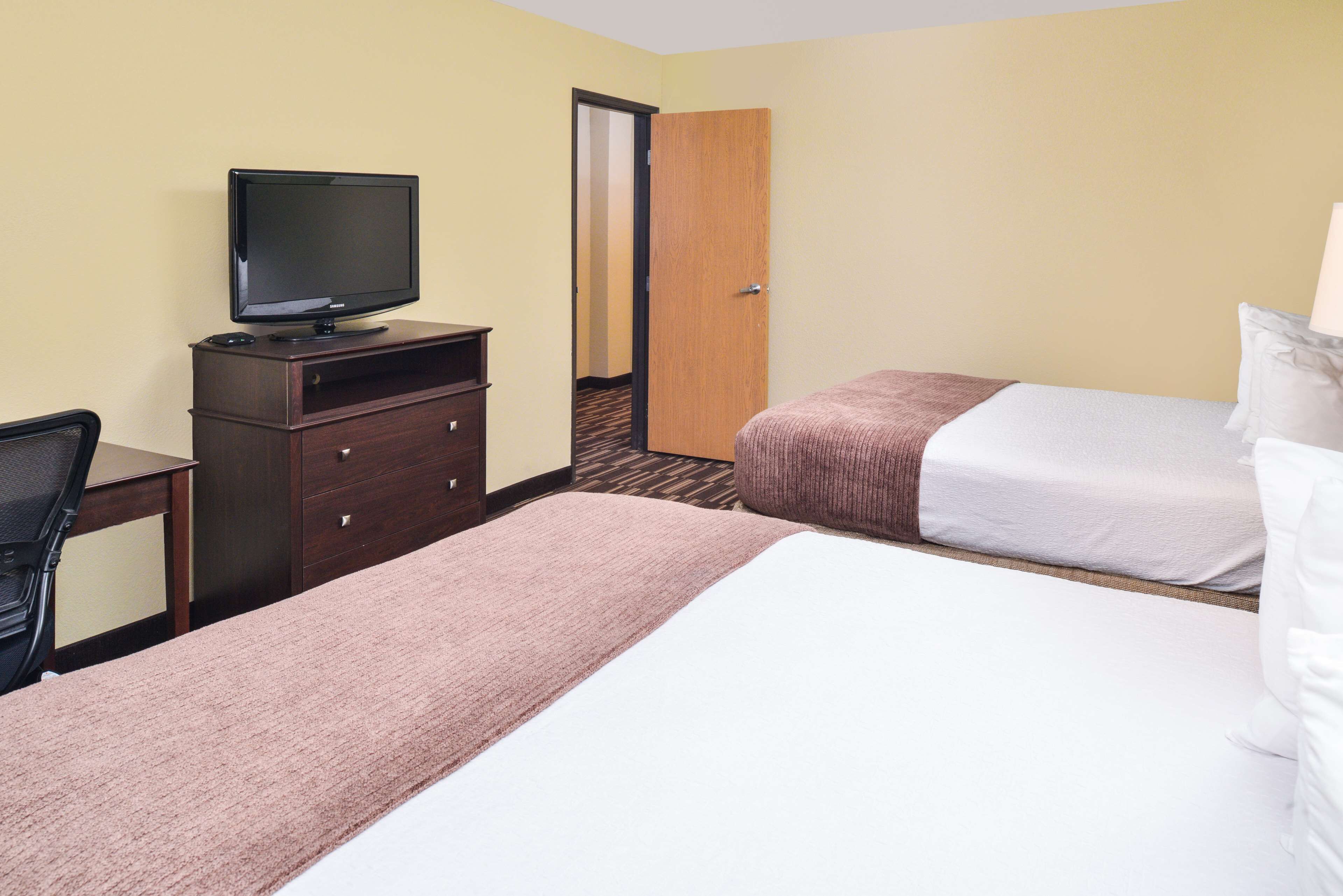 Quarto de hotel com uma cama, uma escrivaninha com televisão, cómoda e porta para outro espaço.