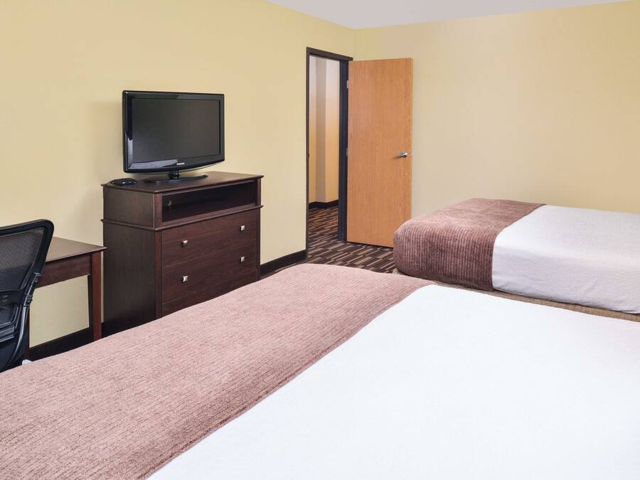 Quarto de hotel com uma cama, uma escrivaninha com televisão, cómoda e porta para outro espaço.