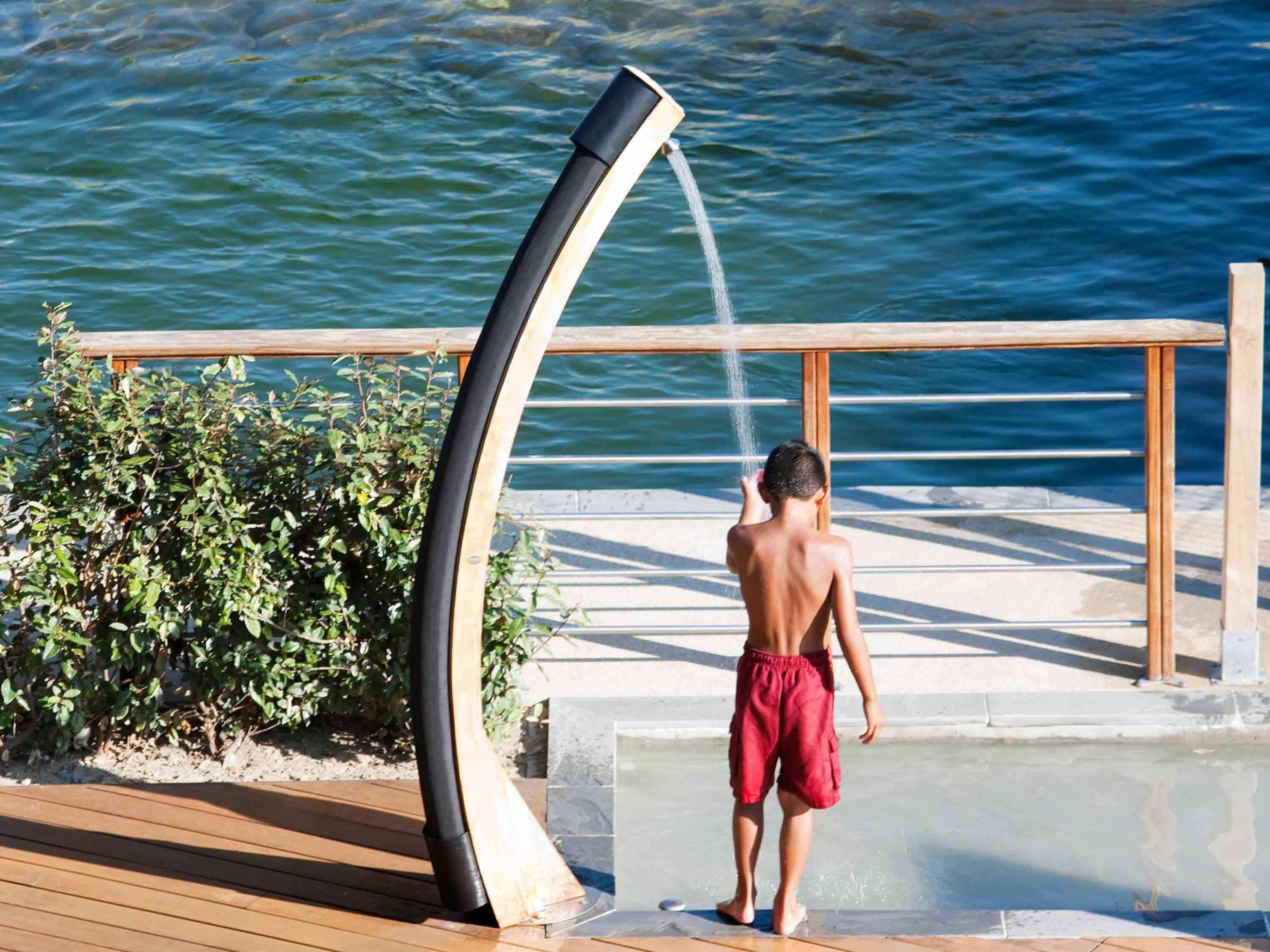 Uma pessoa ao lado de um espelho d'água com uma estrutura curva e um deck de madeira.