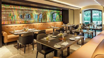 Um restaurante moderno com assentos de couro, uma parede colorida e abstrata, e vista para o verde lá fora.