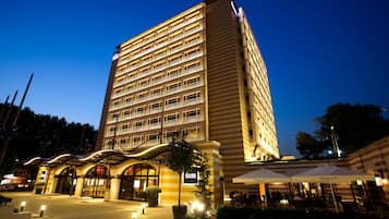 Hotel com fachada moderna, várias varandas e área de entrada bem iluminada com mesas ao ar livre.