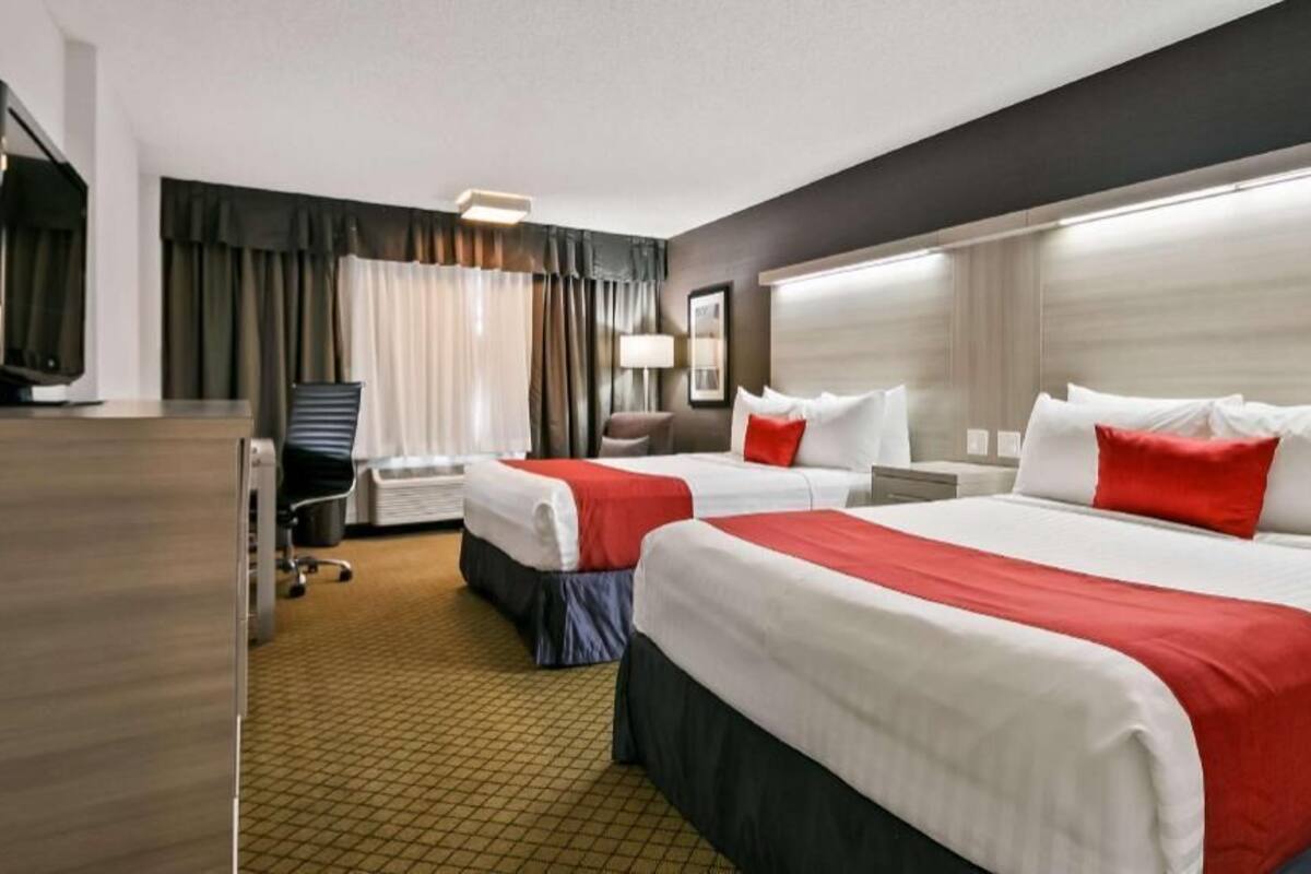 Quarto de hotel com duas camas, uma escrivaninha, uma cadeira, uma televisão e uma janela com cortinas.