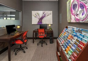 Um espaço de escritório moderno com uma mesa, duas cadeiras de escritório, um computador, uma luminária e uma estante com livros de viagem.
