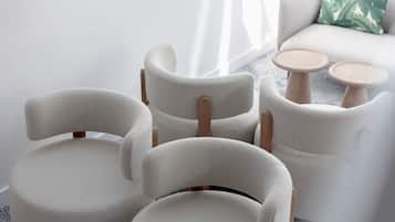 Uma sala de estar moderna com um sofá branco, duas mesas laterais de madeira e três cadeiras estofadas com pés de madeira.