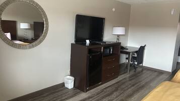 Quarto de hotel com cômoda de madeira escura, televisão de tela plana, escrivaninha com luminária, cadeira e cama com colcha amarela.