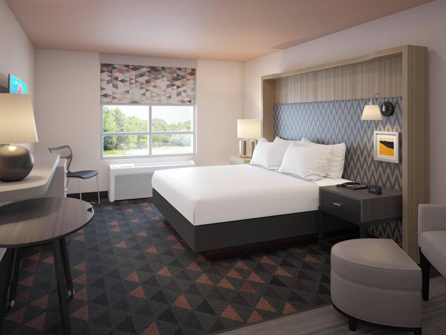 Quarto de hotel com cama, mesas de cabeceira, escrivaninha, cadeira, janela com vista e carpete estampado.
