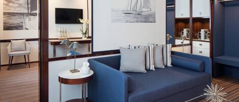 Quarto de hotel moderno com um sofá azul, uma mesa redonda pequena, uma TV de tela plana e um espelho grande.