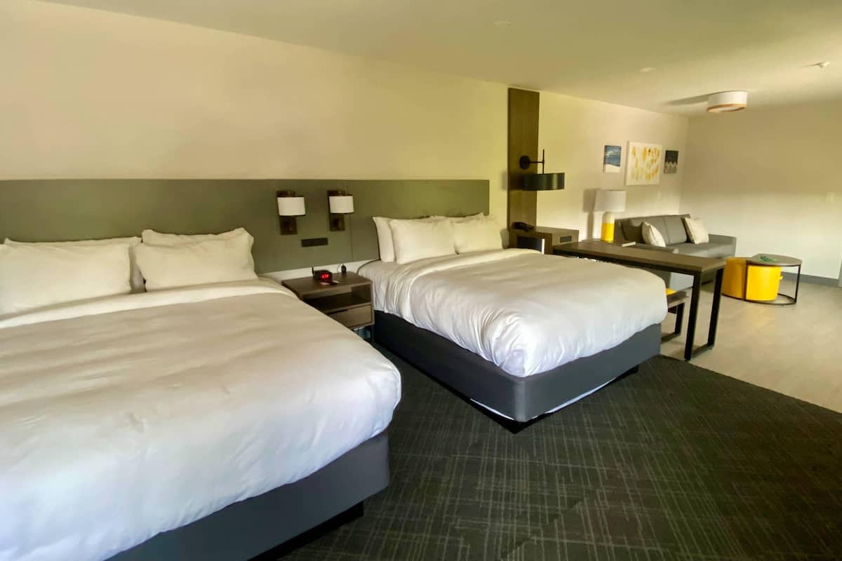 Quarto de hotel com duas camas, uma escrivaninha, uma cadeira, um abajur e uma lixeira.