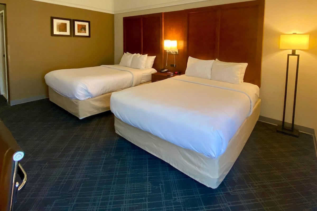 Quarto de hotel com duas camas, mesa de cabeceira com abajur e telefone fixado na parede.