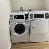 Duas máquinas de lavar roupa de carregamento frontal empilhadas, com mostradores digitais, uma tomada e um tomacorrente na parede.