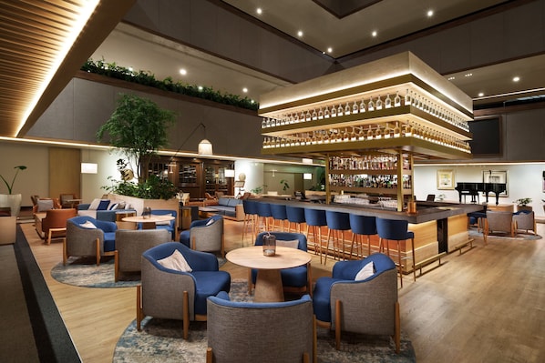 Uma área de bar moderna com pé-alto, detalhes em madeira e diversas opções de assento, incluindo mesas redondas e banquetas.