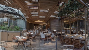 Restaurante com ripas de madeira no teto, plantas em vasos e diferentes opções de assentos.