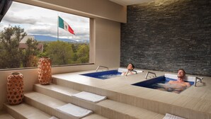 Uma área de spa com duas banheiras de hidromassagem, vista para a cidade e uma parede de pedra.