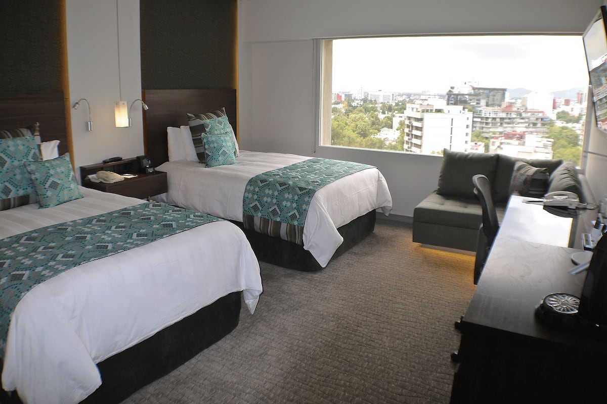 Quarto de hotel com duas camas, uma escrivaninha e vista para a cidade.