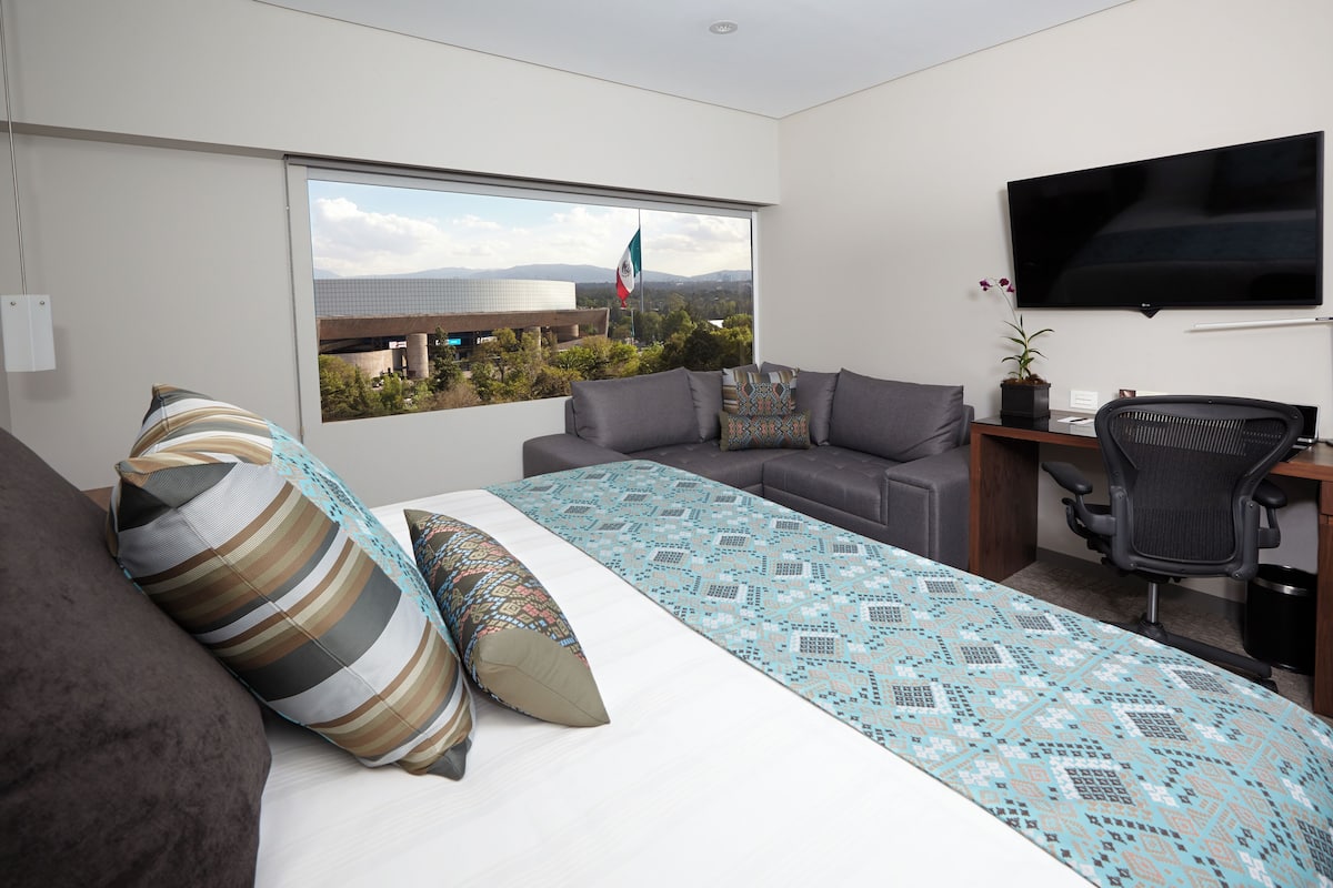 Quarto de hotel com cama grande, sofá, escrivaninha e televisão.