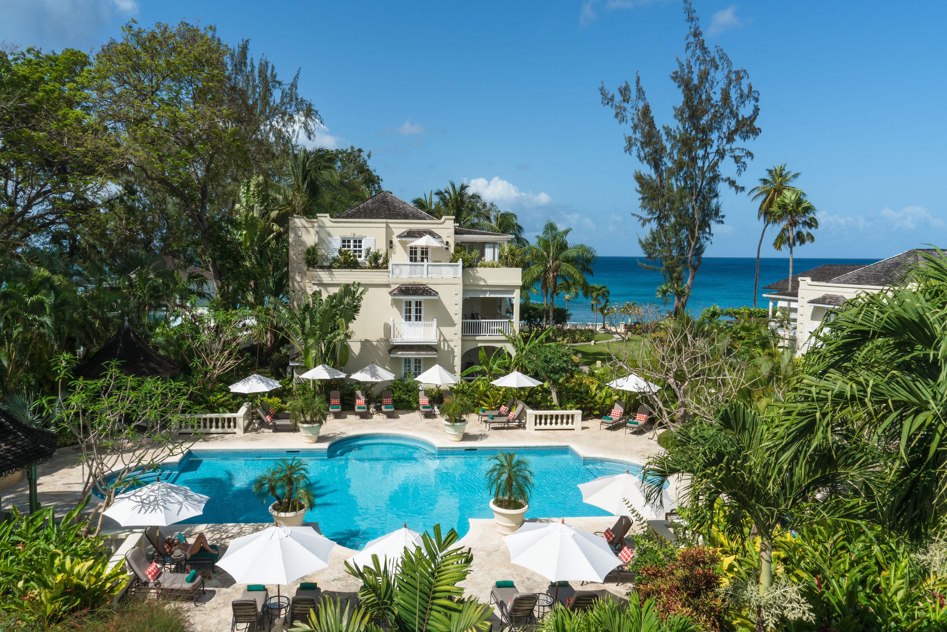 Um resort com piscina, espreguiçadeiras, guarda-sóis e vista para o oceano.