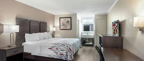 Quarto de hotel com cama, mesas de cabeceira, escrivaninha, cadeira e banheiro com pia, além de uma porta que dá para outro quarto.
