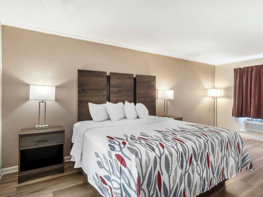Quarto de hotel com cama, duas mesas de cabeceira com abajures, cabeceira e uma janela com cortinas.