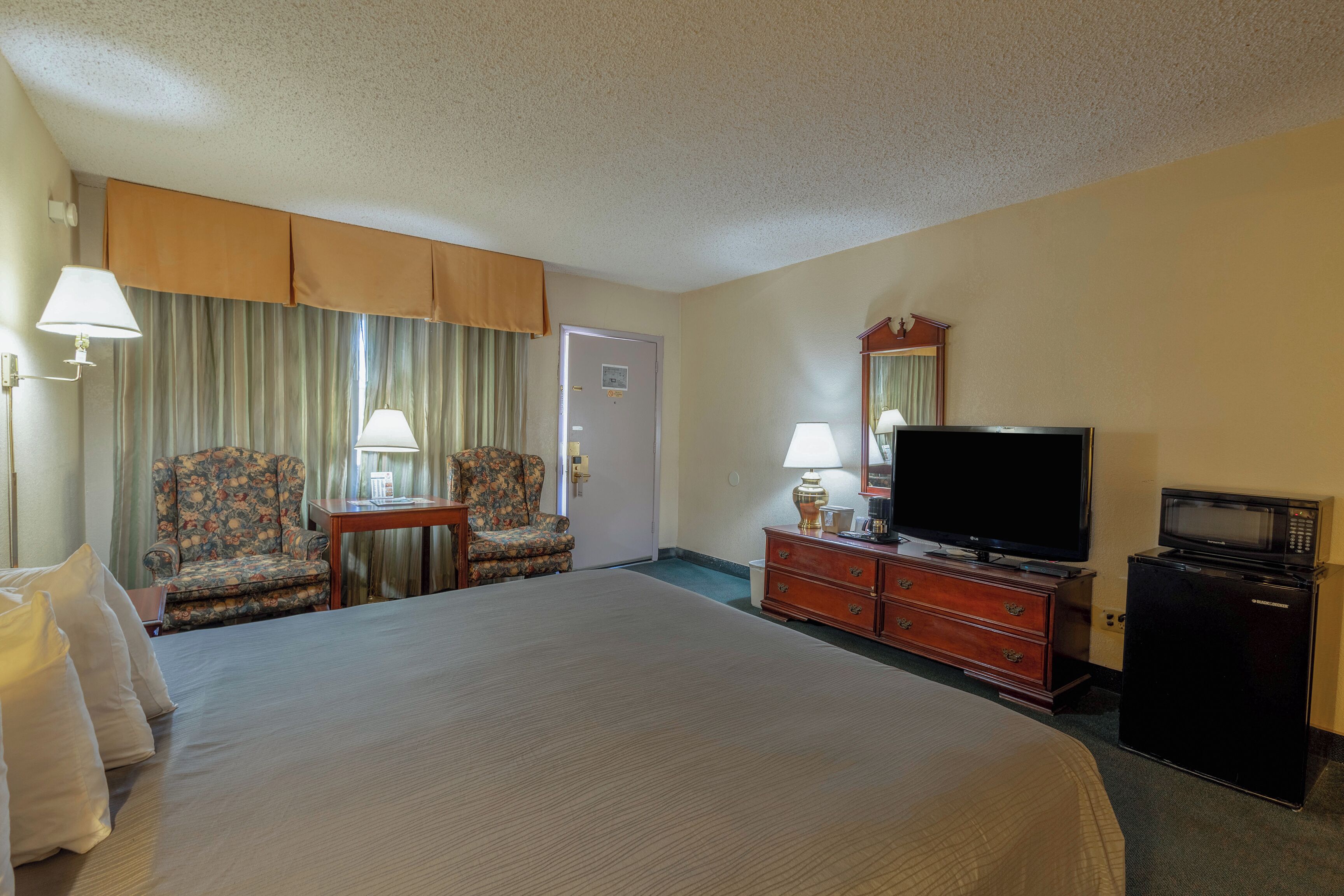 Quarto de hotel com cama grande, duas poltronas, televisão, cômoda e micro-ondas.