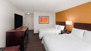 Quarto de hotel com cama, mesa de cabeceira, luminária, televisão e um quadro na parede.
