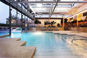Piscina interna com cascata, cercada por áreas de estar e plantas em vasos.