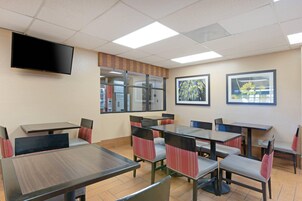 Interior de restaurante com várias mesas e cadeiras, uma TV de tela plana na parede e quadros decorativos nas paredes.