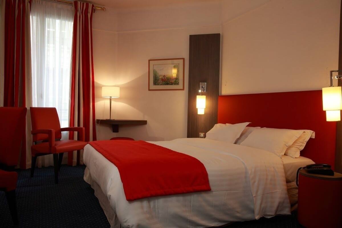 Quarto de hotel com cama, escrivaninha, cadeira e abajur.