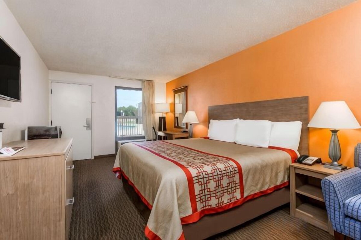 Quarto de hotel com cama, mesas de cabeceira, escrivaninha, cadeira e televisão.