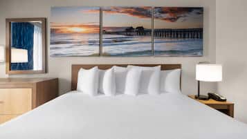 Quarto de hotel com cama, mesa de cabeceira com abajur, telefone e pintura na parede de um pôr do sol sobre o oceano.