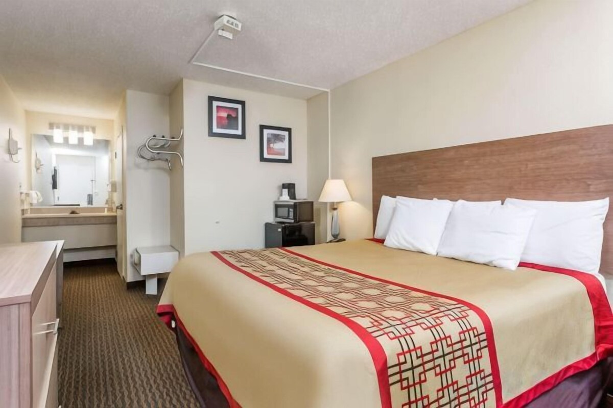 Quarto de hotel com cama, escrivaninha, cadeira, abajur e espelho.