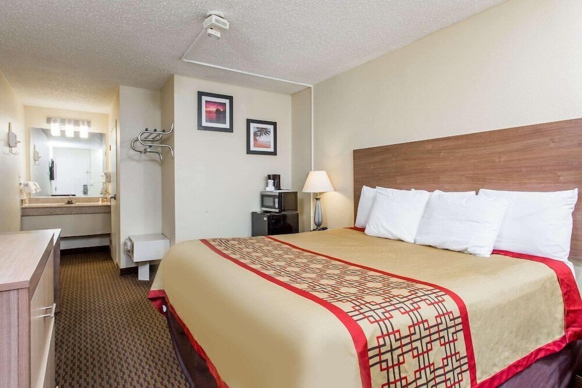 Quarto de hotel com uma cama grande, uma escrivaninha, uma cadeira, uma televisão e um banheiro.