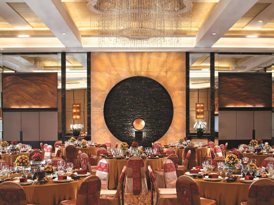 Uma sala de banquetes com mesas redondas, cadeiras e um grande candelabro.