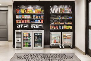 Uma área de máquinas de venda automática com diversas opções de lanches e um refrigerador.