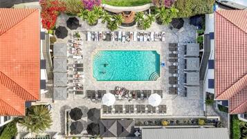 Vista aérea de um resort com piscina central, espreguiçadeiras, guarda-sóis e um jardim bem cuidado.