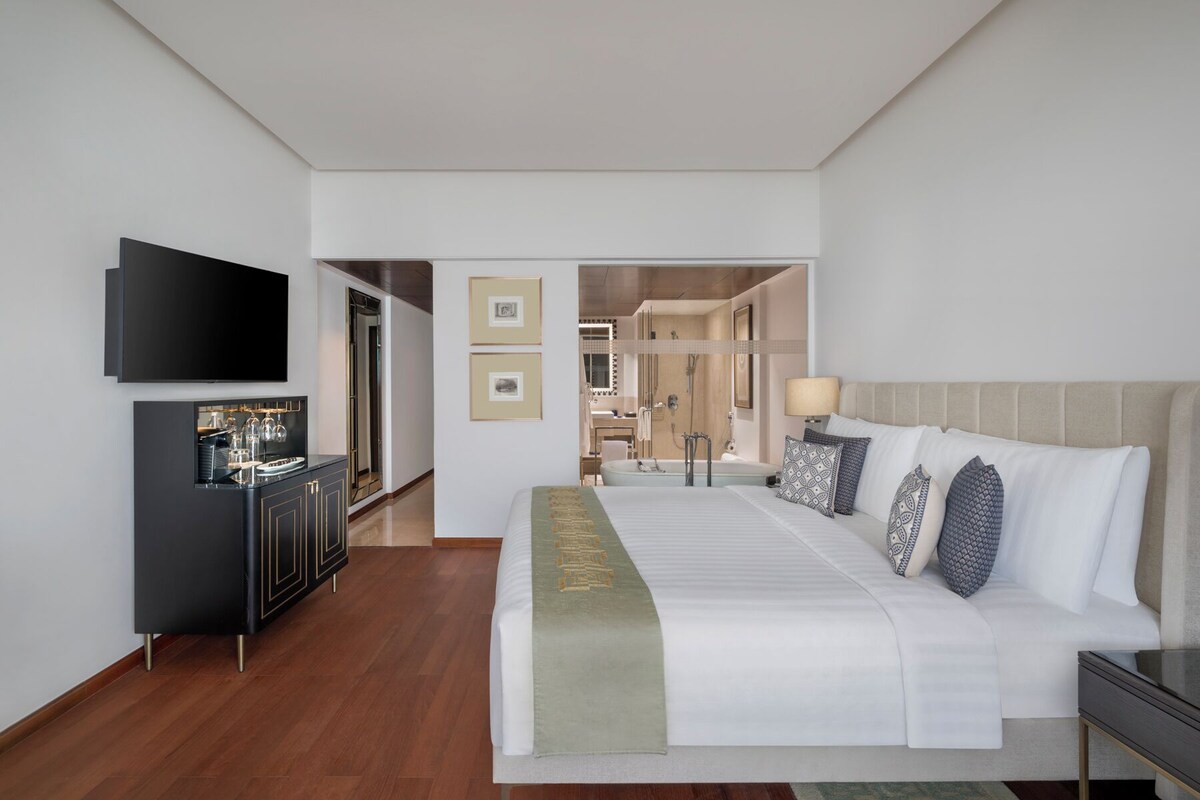 Quarto de hotel com cama, mesa de cabeceira, televisão e vista para o banheiro.