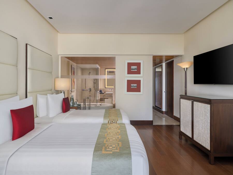 Quarto de hotel com uma cama grande, uma televisão, um armário e um banheiro visível por uma porta aberta.