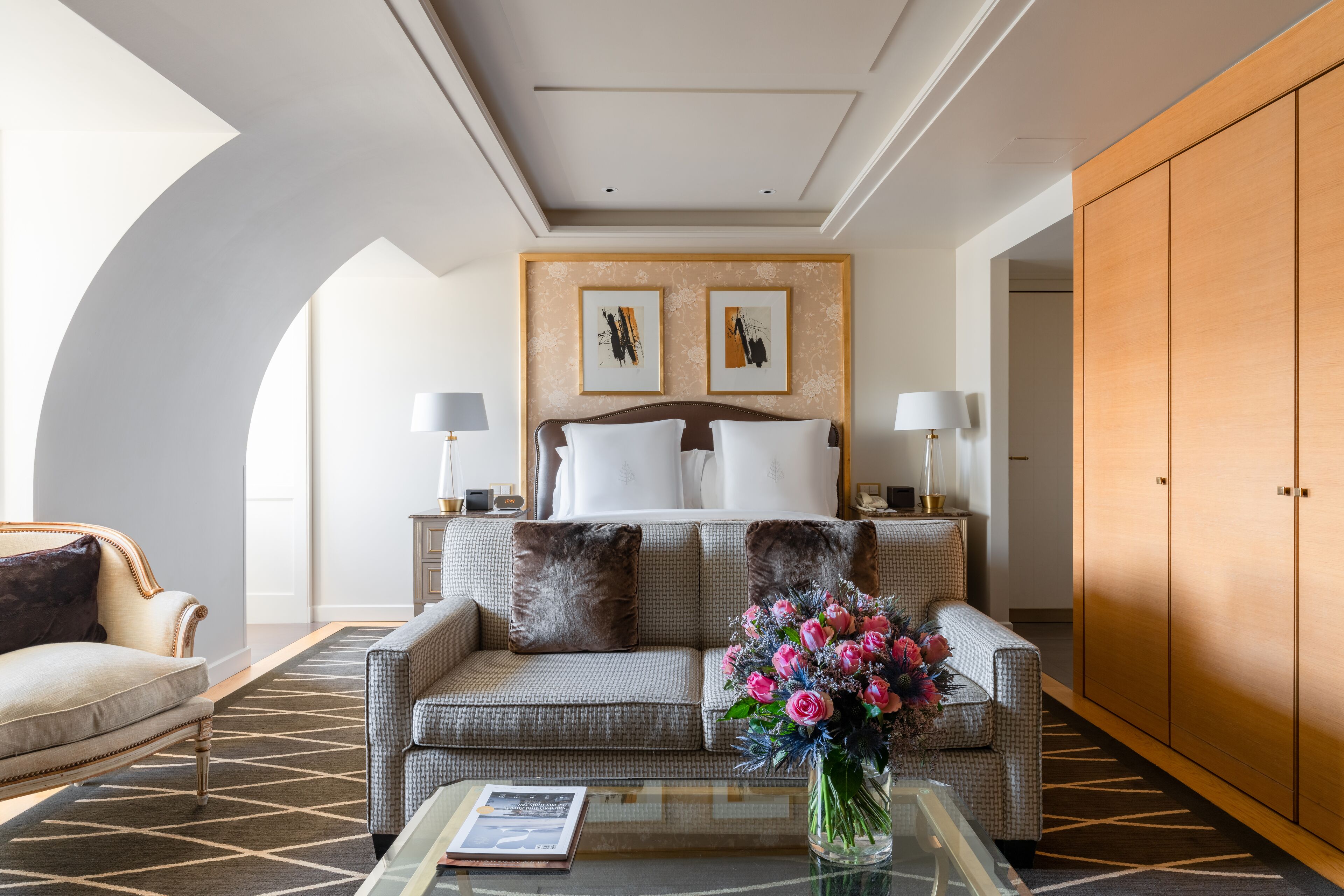Quarto de hotel com uma cama, um sofá, uma mesa de centro com um vaso de flores e um guarda-roupa.