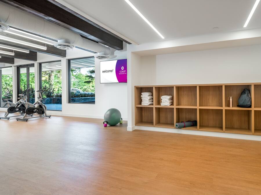 Uma academia com equipamentos de exercício, prateleiras de madeira com toalhas e um letreiro com a palavra 'welcome'.