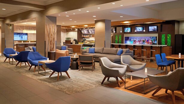 Espaço lounge moderno com sofás, poltronas e um bar com diversas bebidas.