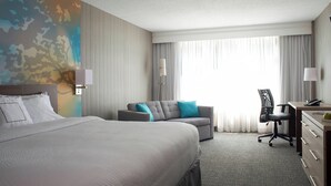 Quarto de hotel com uma cama grande, um sofá, uma escrivaninha com cadeira e uma janela ampla com cortinas.