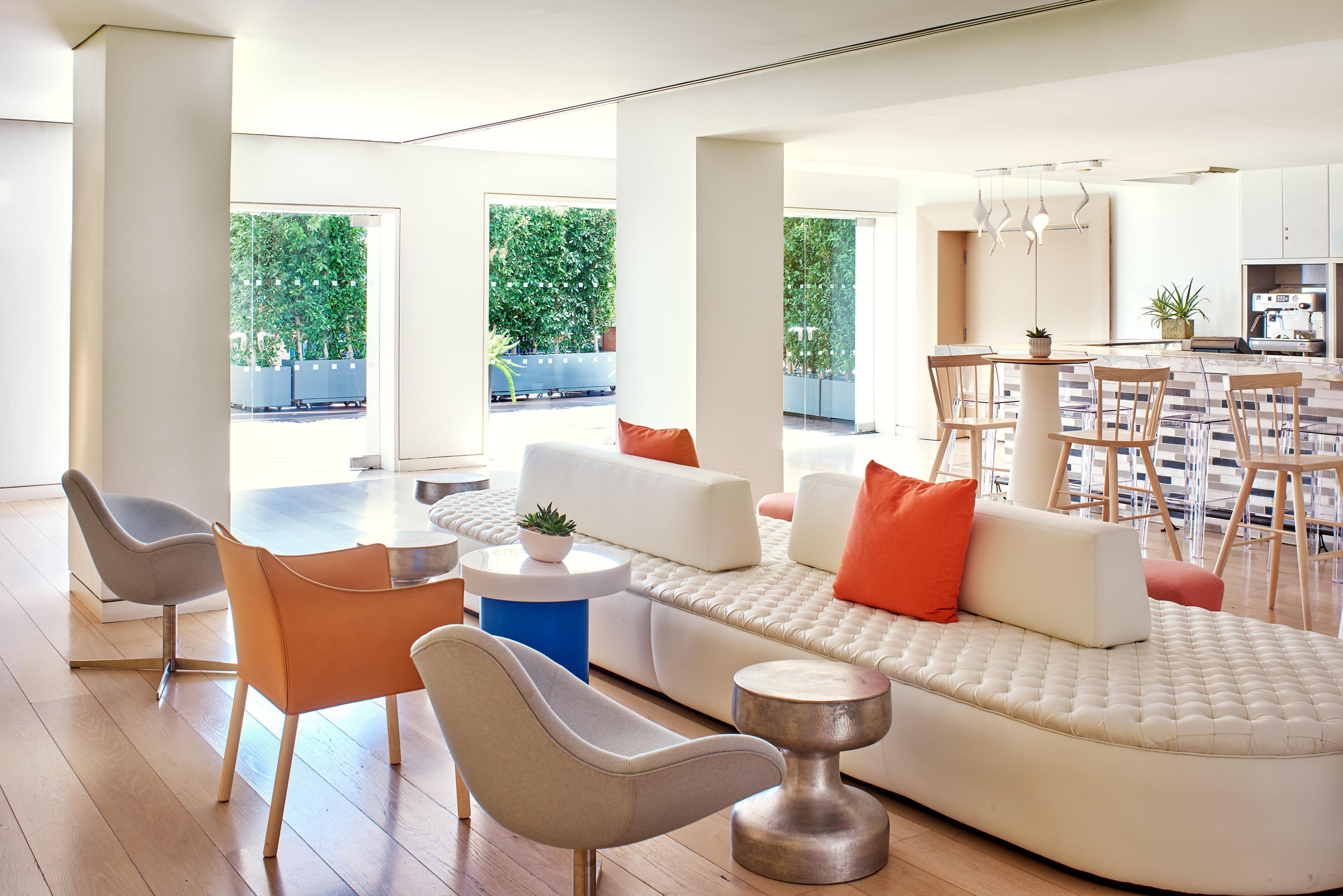 Sala de estar moderna com sofá, cadeiras, mesa de centro e área de cozinha visível através de amplas janelas.