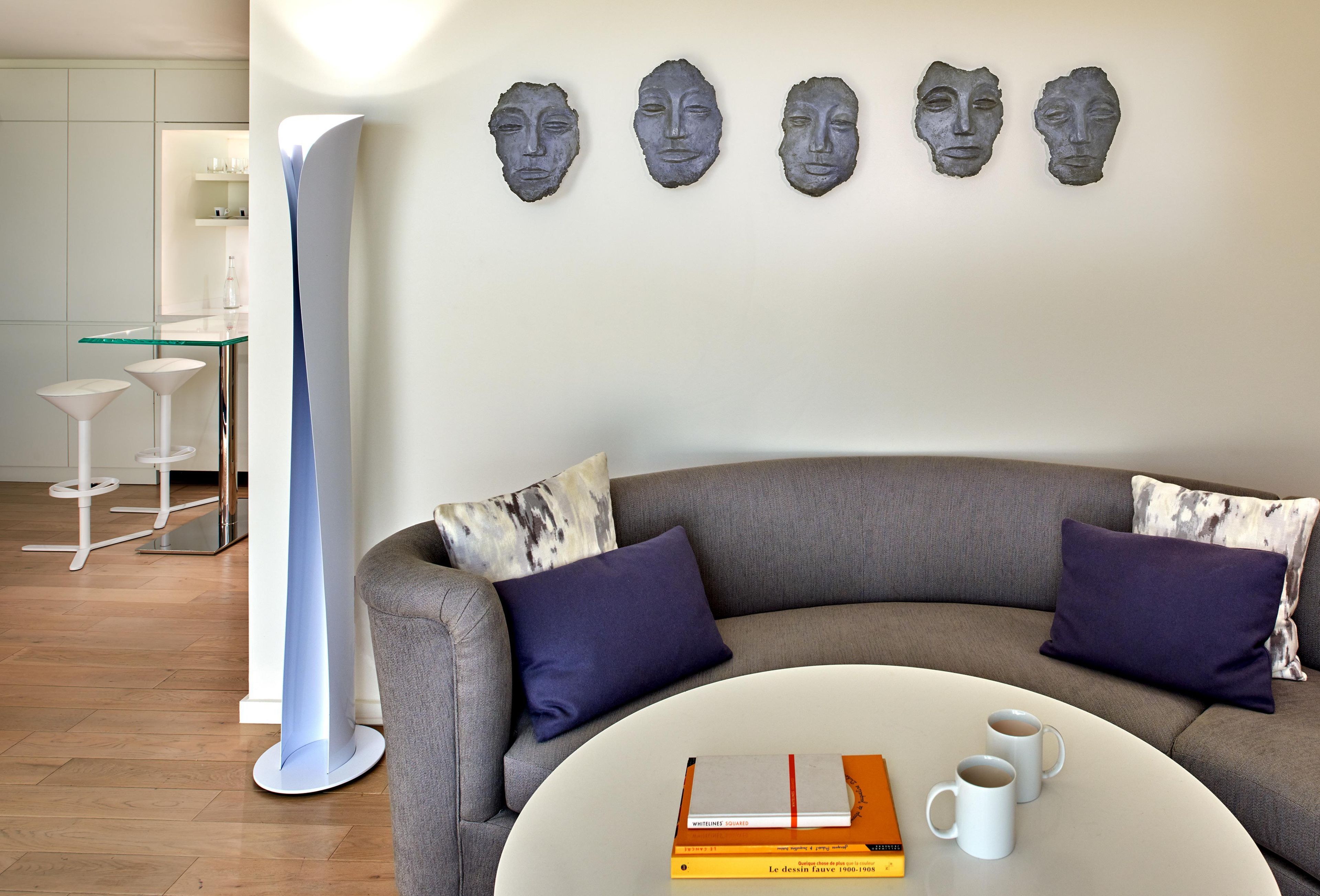 Uma sala de estar moderna com um sofá cinza, duas almofadas roxas, uma mesa de centro de vidro e um livro intitulado 'WHITELINES SQUARED'.