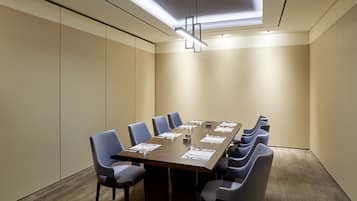 Uma sala de conferências com uma longa mesa, cadeiras azuis e um lustre moderno.