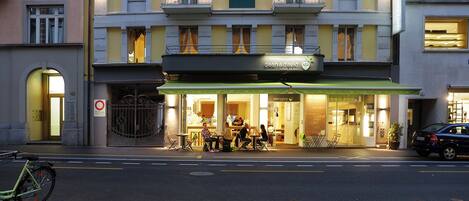 Um restaurante com mesas ao ar livre, uma bicicleta estacionada em frente e um edifício com a placa 'dean & david'.