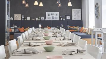 Uma sala de jantar com uma mesa comprida posta para refeição, rodeada por cadeiras brancas.