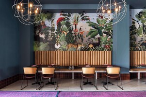 Um restaurante com um longo banco de madeira para acomodação, um mural com vida selvagem tropical e iluminação pendente.