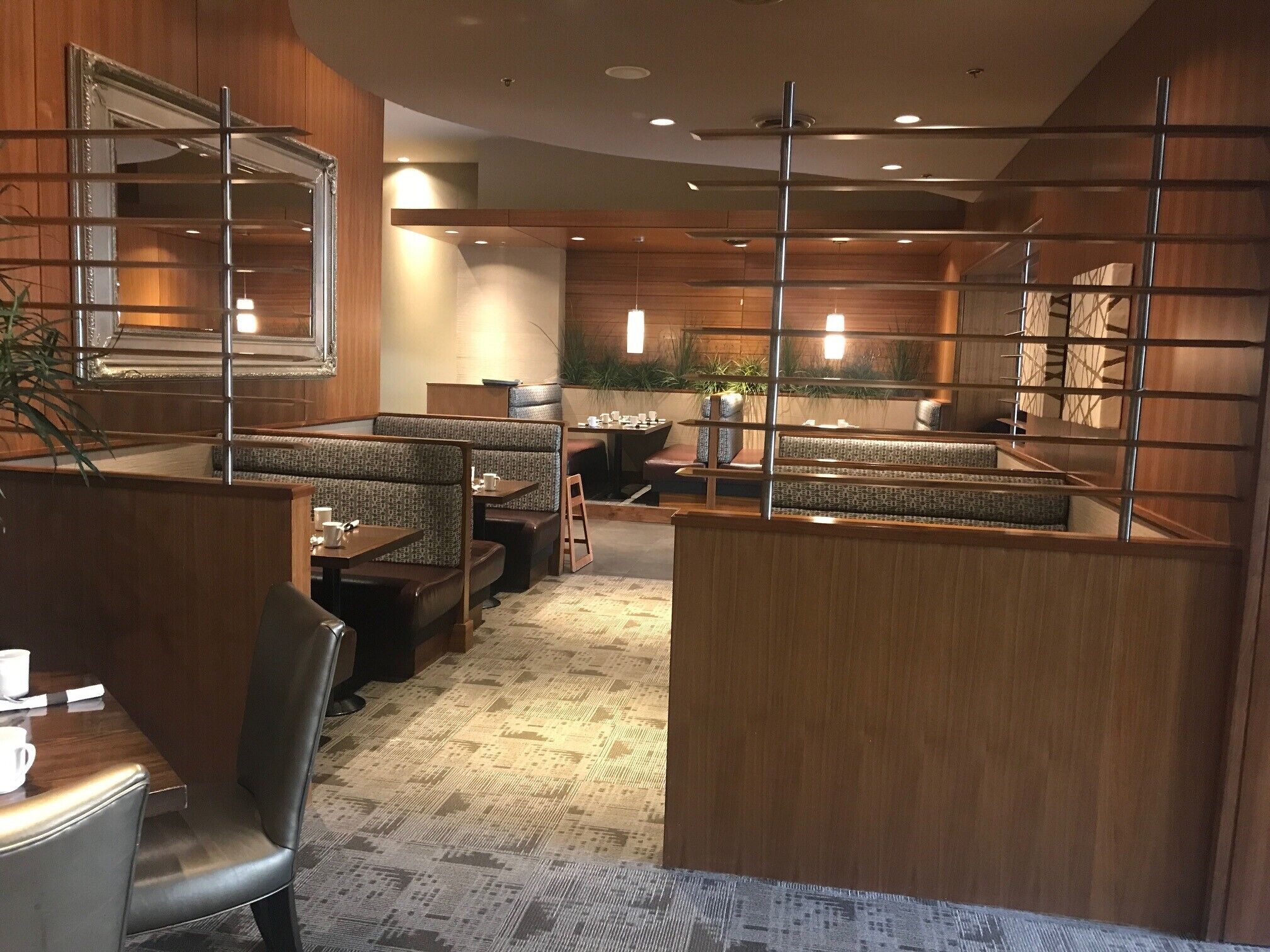 Um restaurante com cabines e mesas, painéis de madeira e plantas.