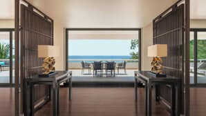 Um interior moderno com vista para o oceano, apresentando uma área de jantar com mesa e cadeiras, e duas mesas laterais com luminárias.